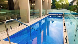 Uma piscina interior moderna com paredes de vidro transparente, chão em azulejo e escada de metal.