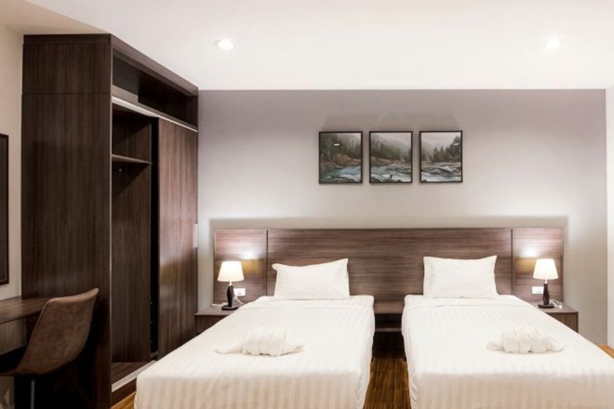 Quarto de hotel com cama de casal, duas mesas de cabeceira com luminárias, um guarda-roupa e três quadros na parede.