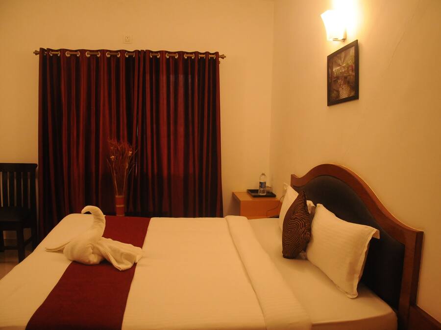 Quarto de hotel com cama, mesa de cabeceira, uma cadeira e luminária fixada na parede.