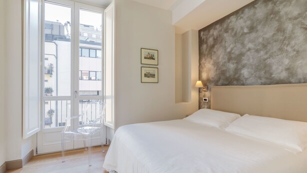 Quarto com uma cama grande, janela com vista para prédios e duas quadros na parede.