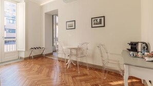 Quarto moderno com piso de madeira em padrão herringbone, porta branca, pequena mesa com cadeiras e área de kitchenette.