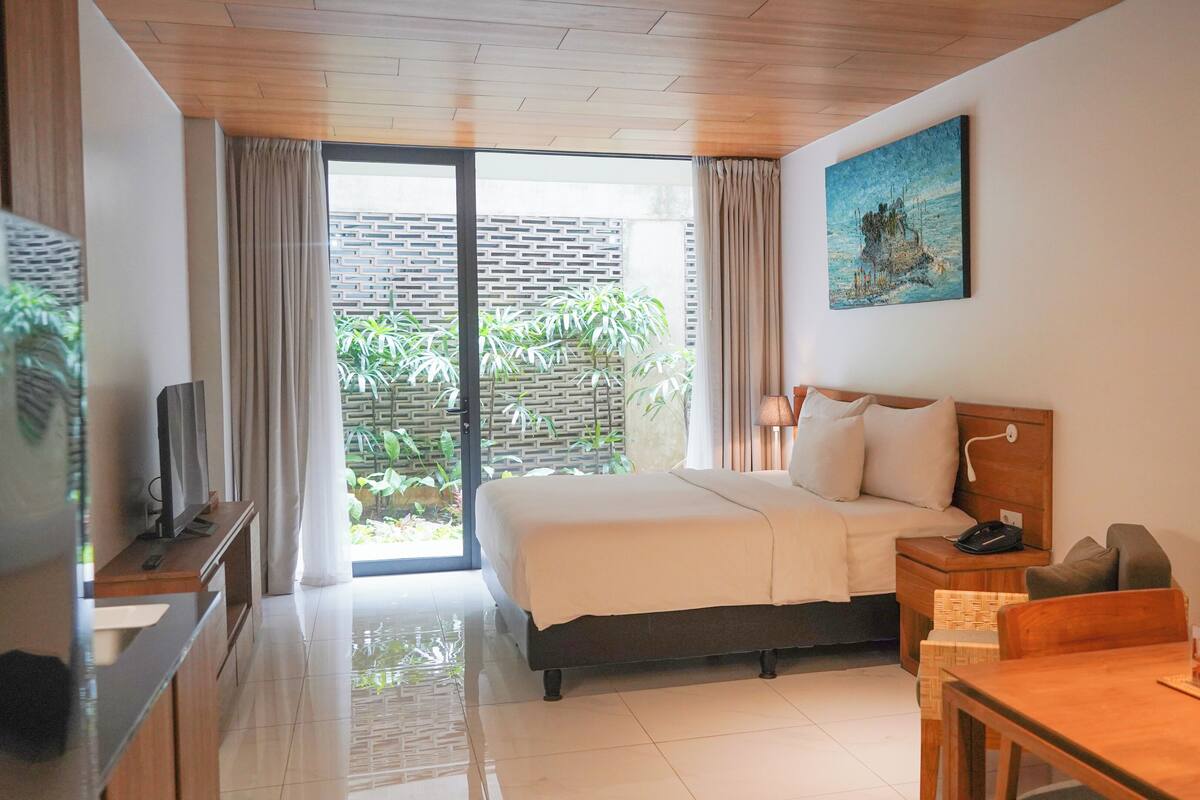 Quarto de hotel com cama, mesa de cabeceira, abajur e um quadro na parede.