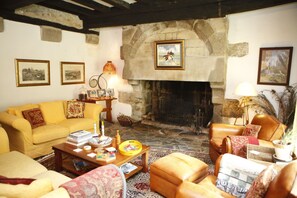 Uma sala de estar acolhedora com lareira de pedra, sofás amarelos e castanhos, e uma mesa de centro com livros e objetos decorativos.