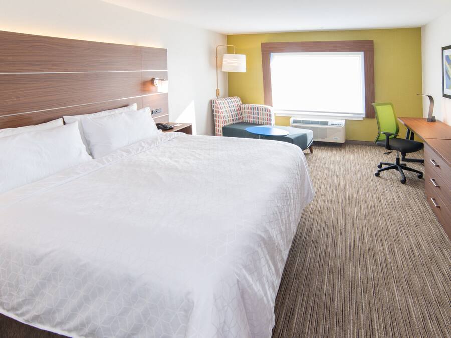 Quarto de hotel com uma cama grande, escrivaninha, cadeira, televisão e janela com persianas.