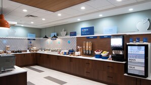 Uma área de café da manhã moderna com um painel de menu digital, diversas estações de comida e uma máquina de café.