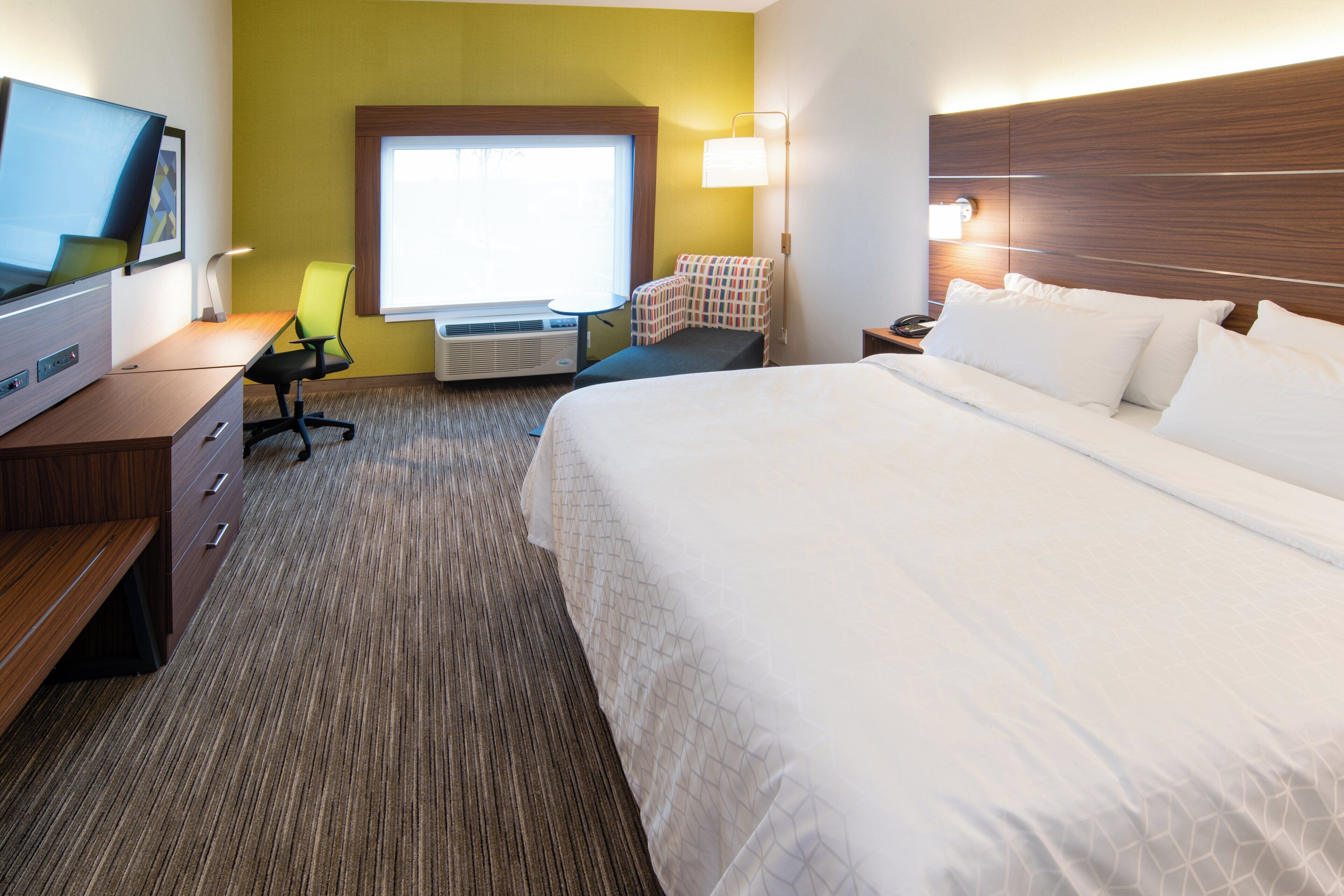 Quarto de hotel com cama, escrivaninha, cadeira, televisão e janela com vista.