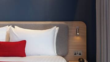 Quarto de hotel com cama, mesa de cabeceira, telefone e tomada na parede.