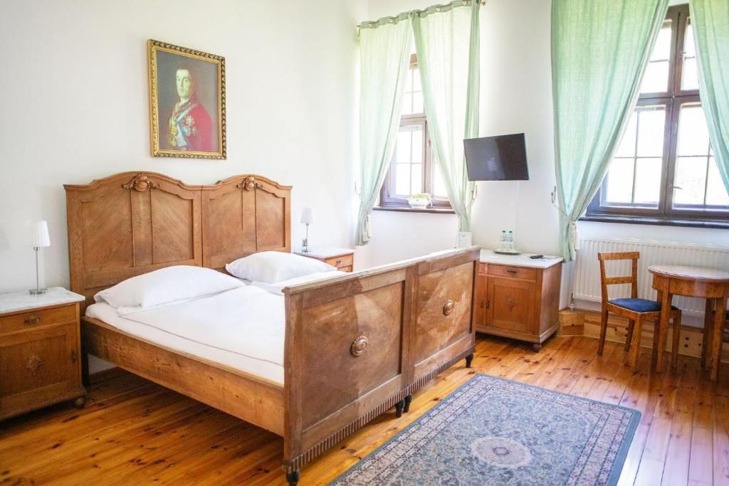 Quarto com cama de madeira, mesa de cabeceira, cadeira, mesinha, televisão e janela com cortinas.