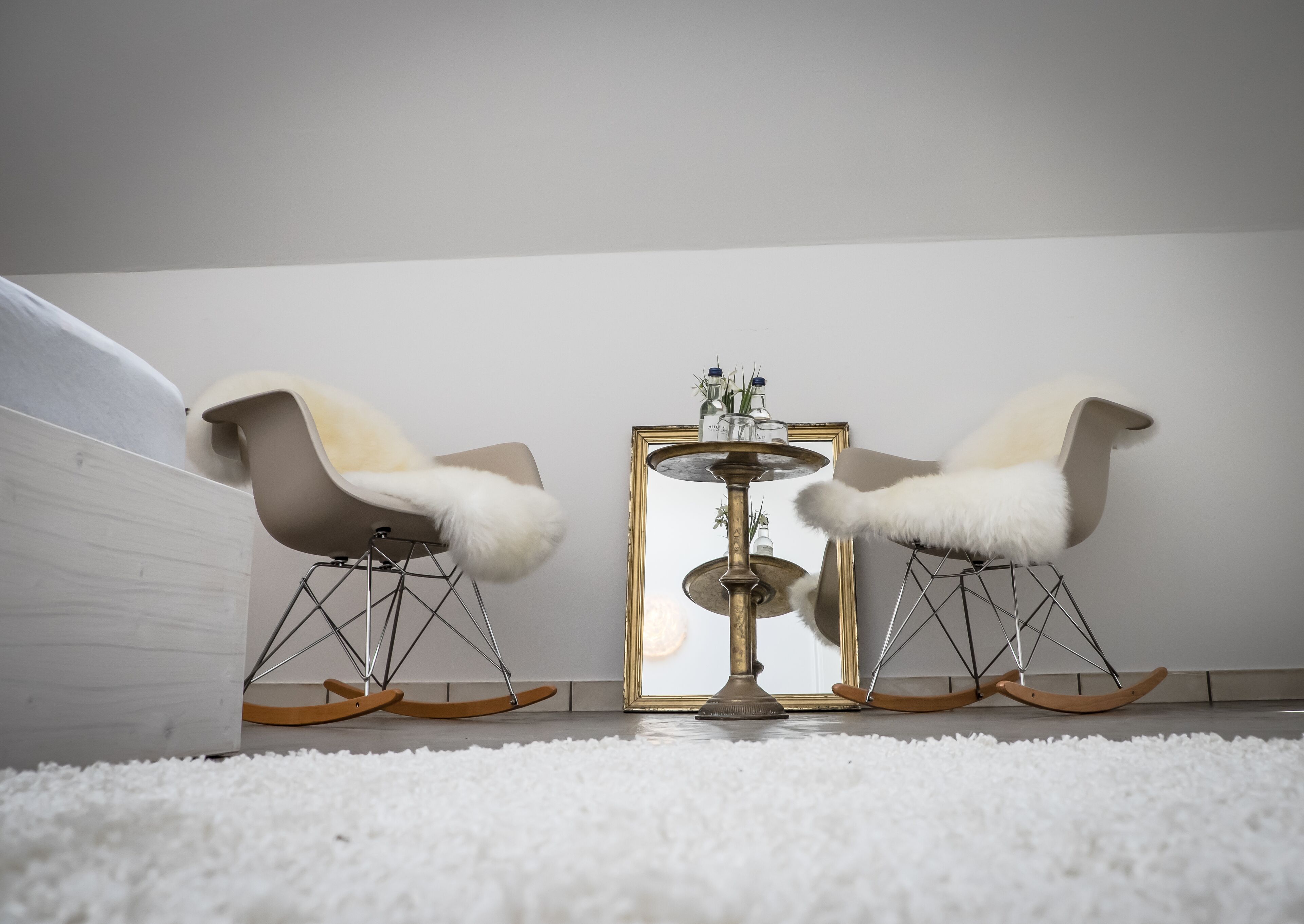 Quarto com duas cadeiras de balanço, uma mesinha com espelho e um tapete branco e fofo.