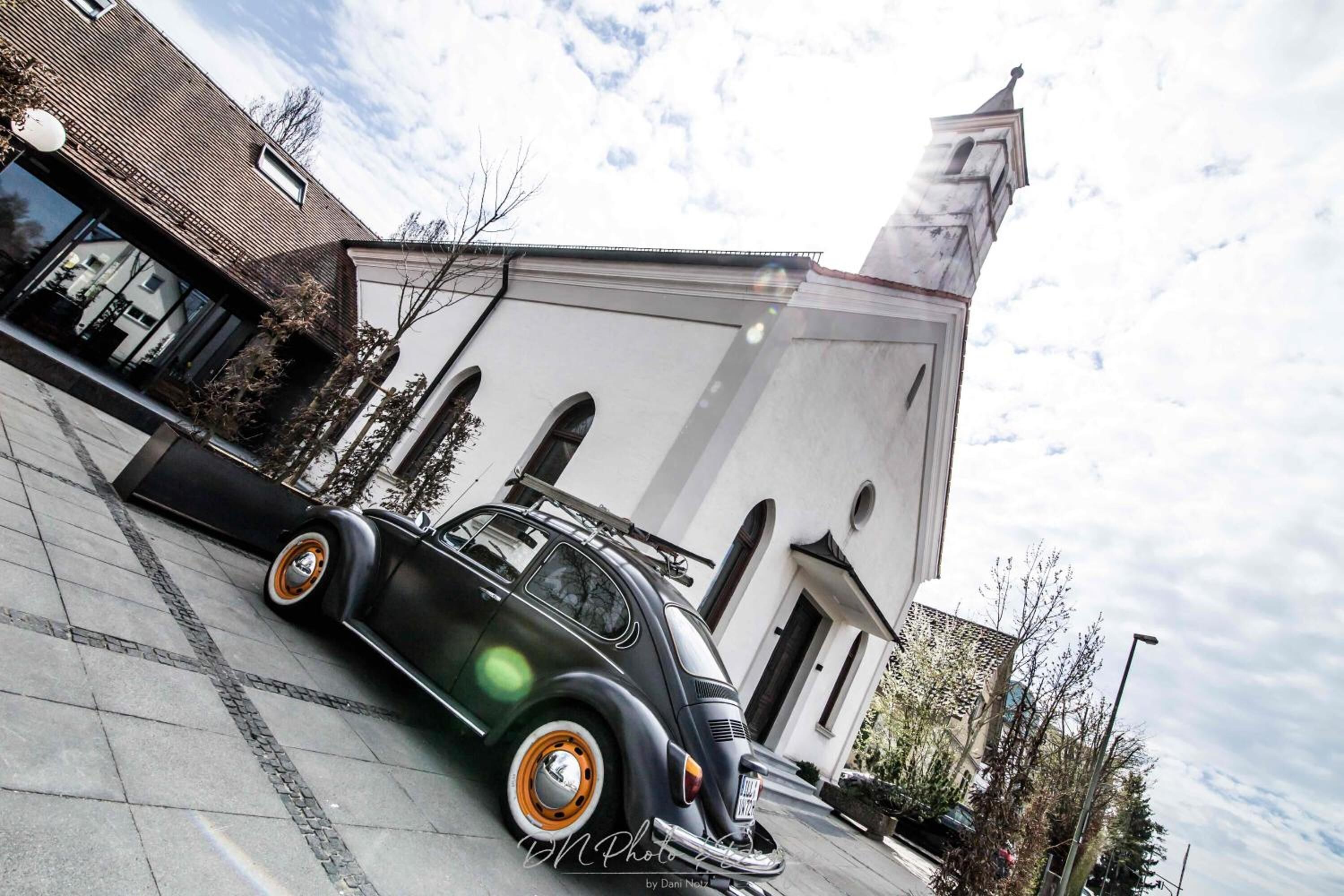 Carro antigo estacionado em frente a um edifício com fachada branca e torre do relógio.
