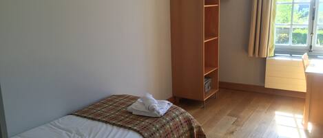 Quarto com uma cama de solteiro, guarda-roupa de madeira, janela com cortinas e radiador.
