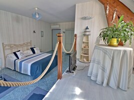 Quarto com cama, escrivaninha com planta, prateleira pequena com objetos decorativos e ventilador de teto.