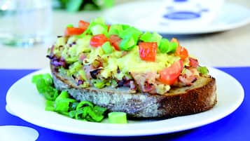 Sanduíche em um prato branco com cebolinha, tomate e outros ingredientes.