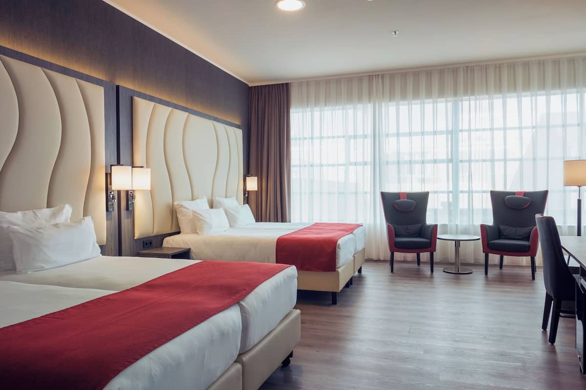 Quarto de hotel com duas camas, uma mesinha e duas cadeiras.