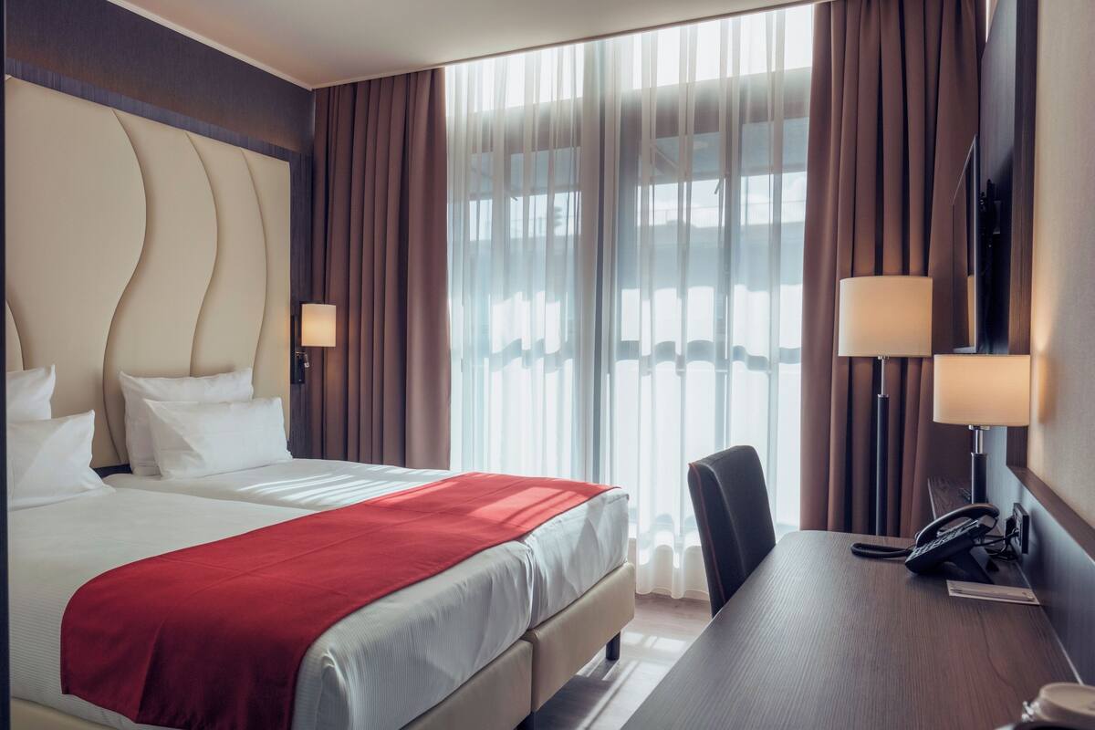Quarto de hotel com uma cama grande, duas mesas de cabeceira, uma escrivaninha e uma cadeira.