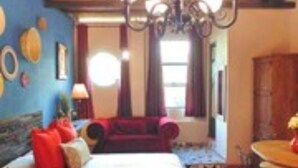 Um quarto com uma cama, um sofá vermelho, uma mesa de jantar com cadeiras e um candelabro.