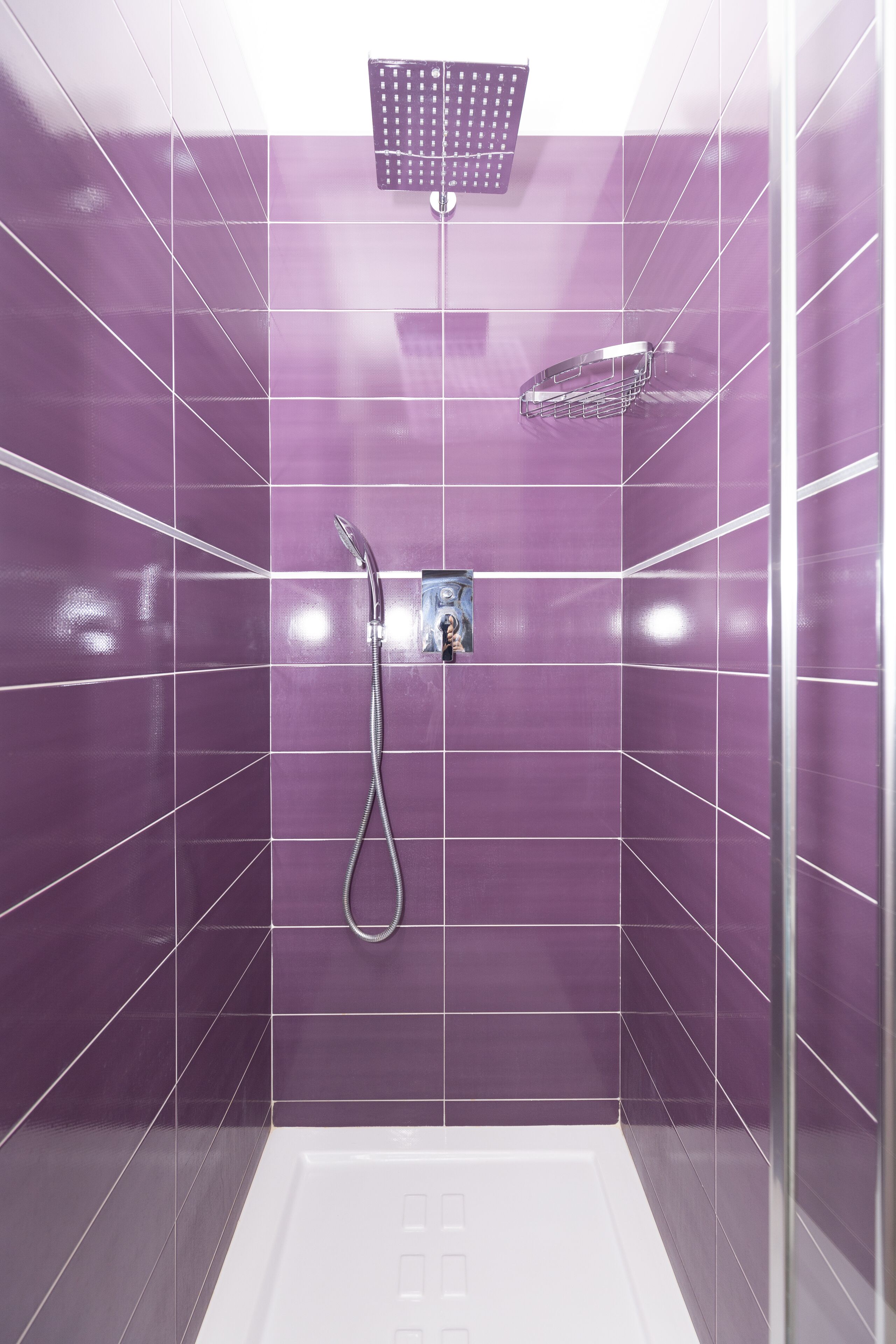 Um banheiro com azulejos roxos, um chuveiro e área de ducha com divisória de vidro.