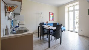 Cozinha moderna com pia, fogão e utensílios. Possui uma área de refeições com mesa e cadeiras. Um sofá é visível ao fundo.