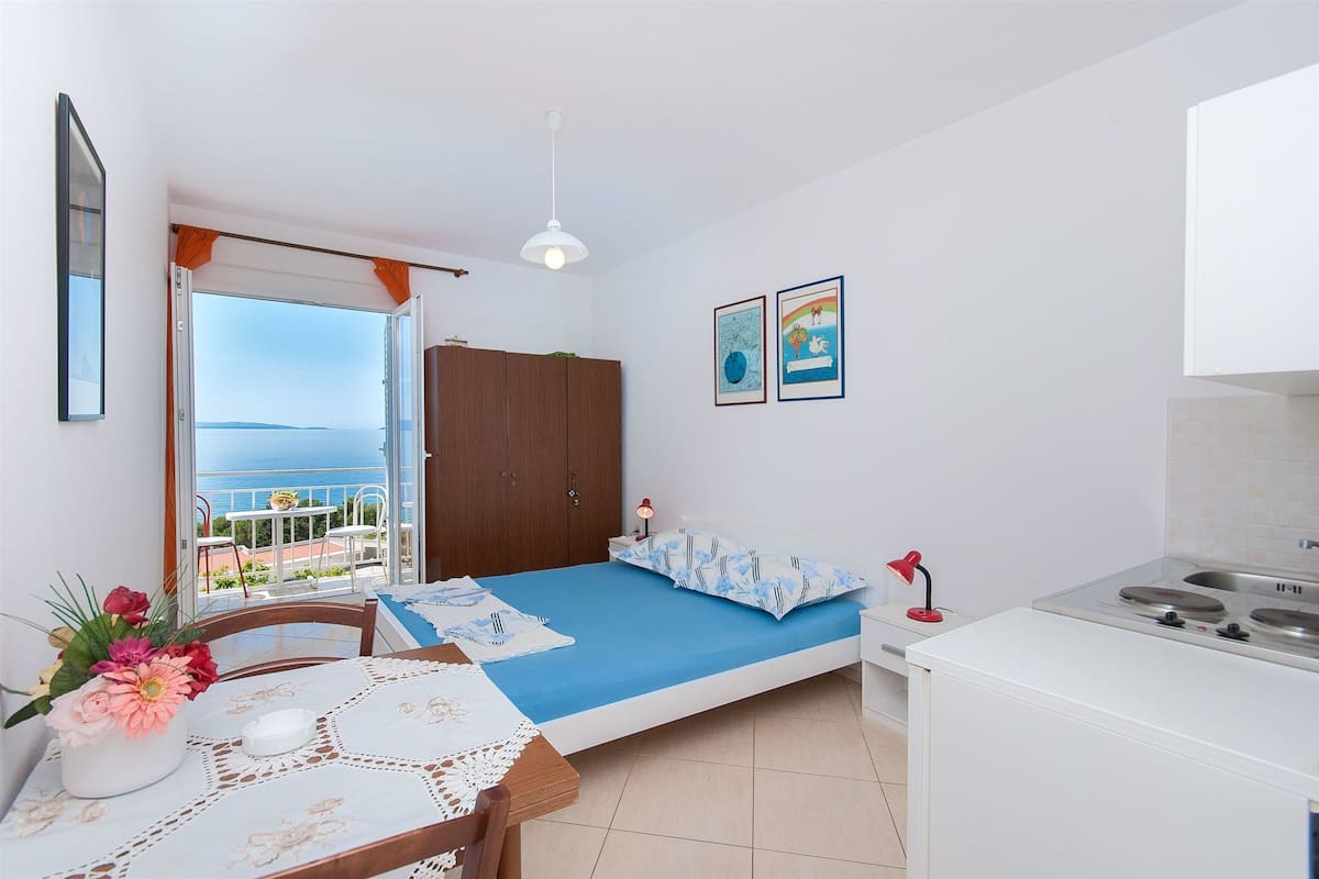Quarto com cama, mesa de cabeceira, escrivaninha, cadeira, janela e vista para o mar.