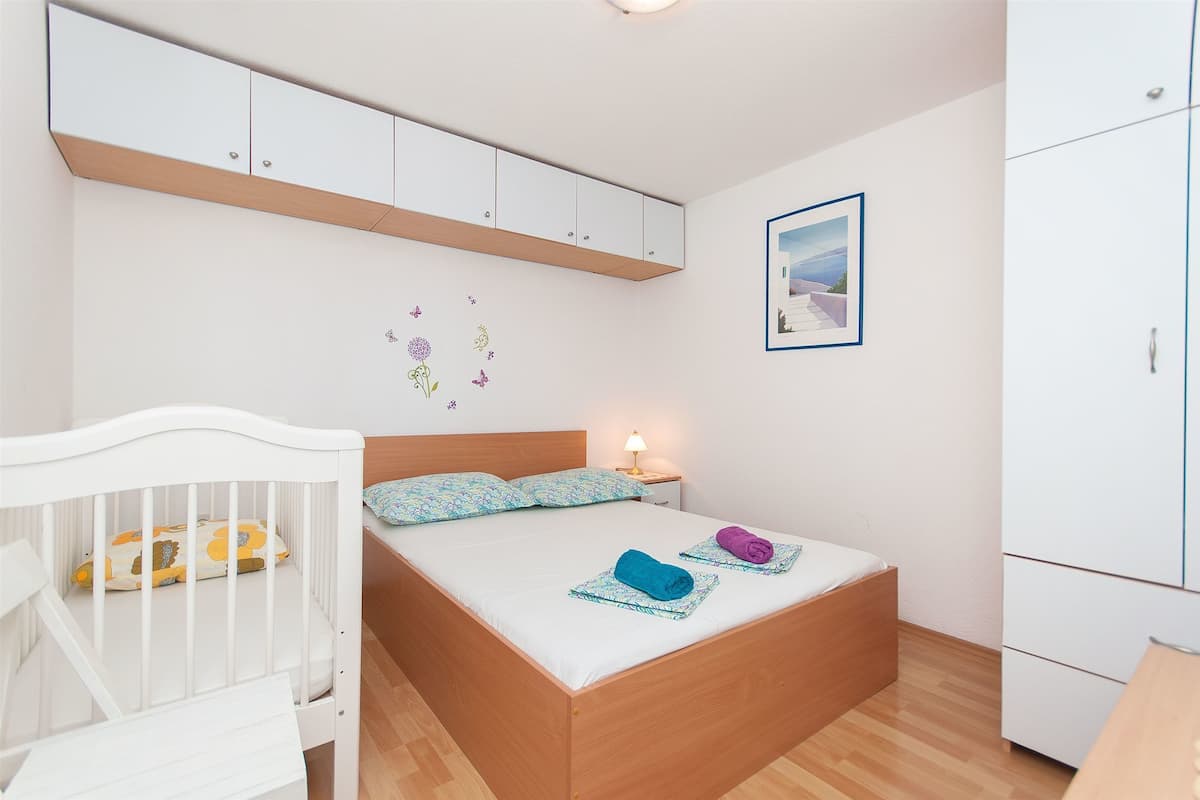 Quarto com cama de madeira, berço, guarda-roupa e um armário fixado na parede.