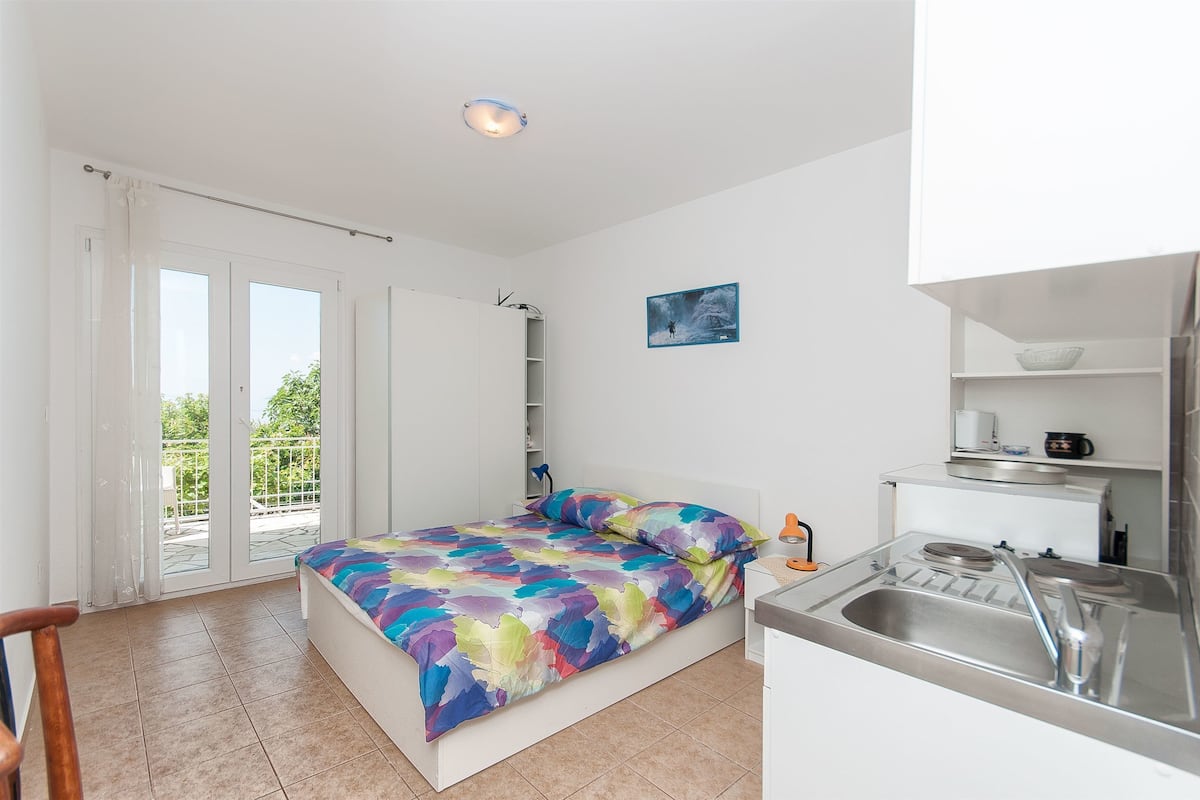 Quarto com cama, banheiro e cozinha compacta.