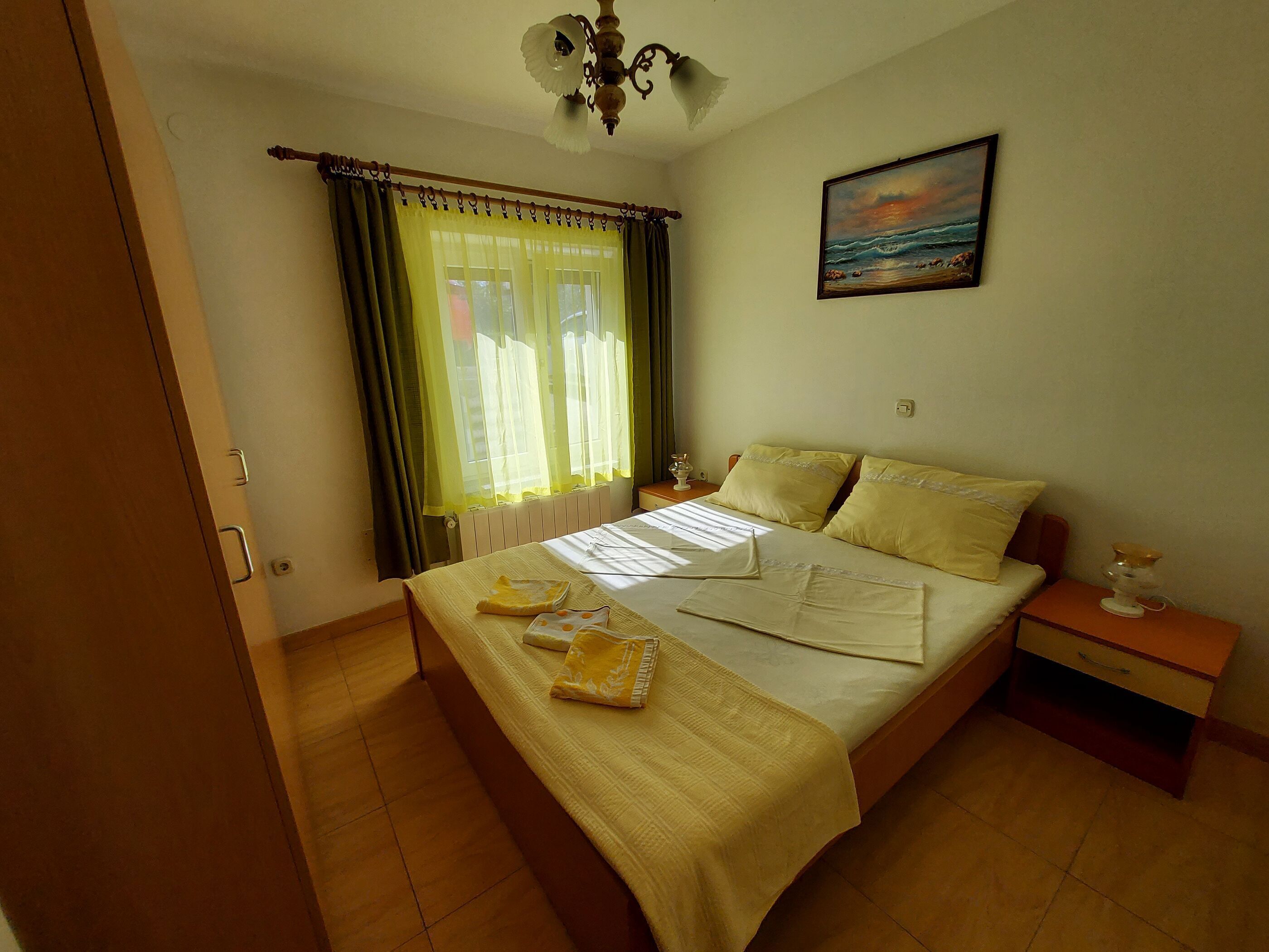 Quarto bem arrumado com cama, mesa de cabeceira, cortinas e um quadro na parede.