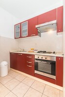 Uma cozinha compacta com armários vermelhos, um fogão de aço inoxidável e painel de azulejos.