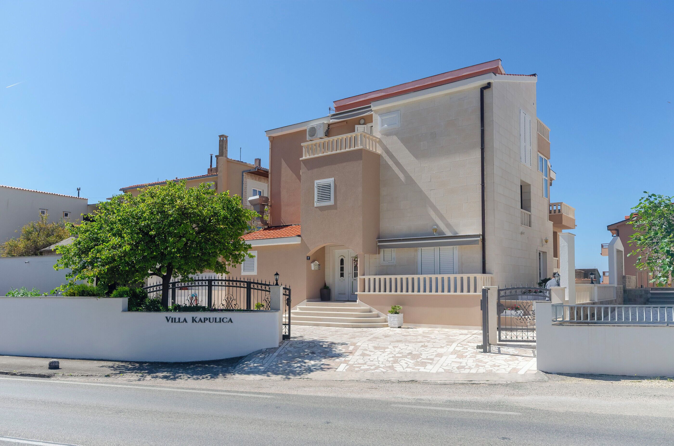 Uma villa moderna com fachada bege, telhado vermelho e entrada com portão.