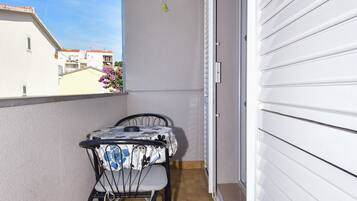 Uma varanda com mesa e cadeiras, uma porta de correr e um aparelho de ar condicionado.
