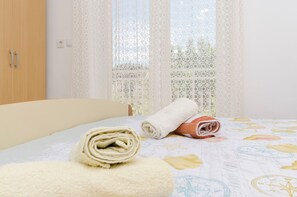 Uma cama com uma toalha branca enrolada, uma toalha laranja enrolada e uma toalha branca fofa sobre um edredom com padrão de bússola.