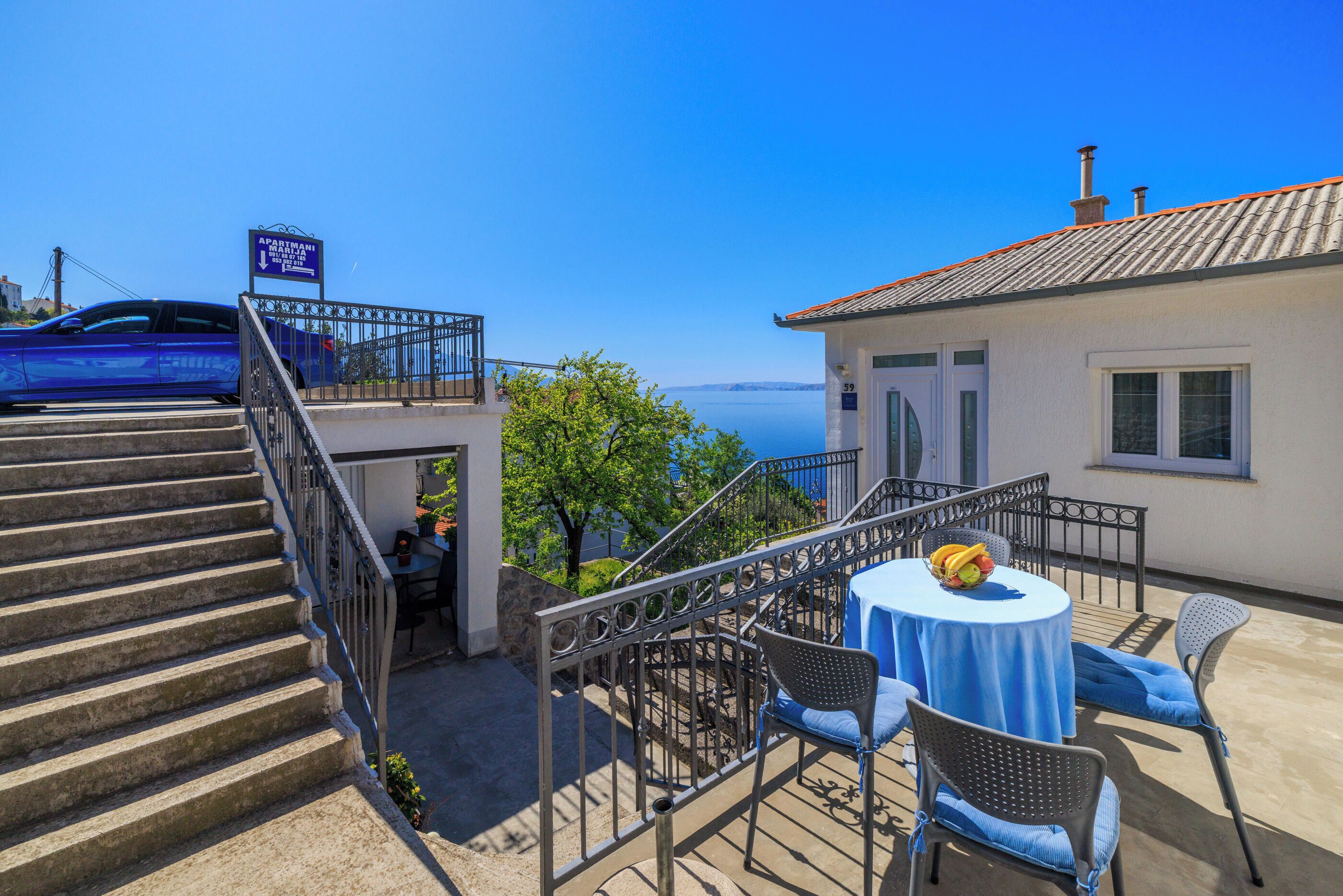 Um terraço com mesa, cadeiras, escadaria e vista para o mar.