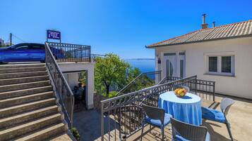 Um terraço com mesa, cadeiras, escadaria e vista para o mar.
