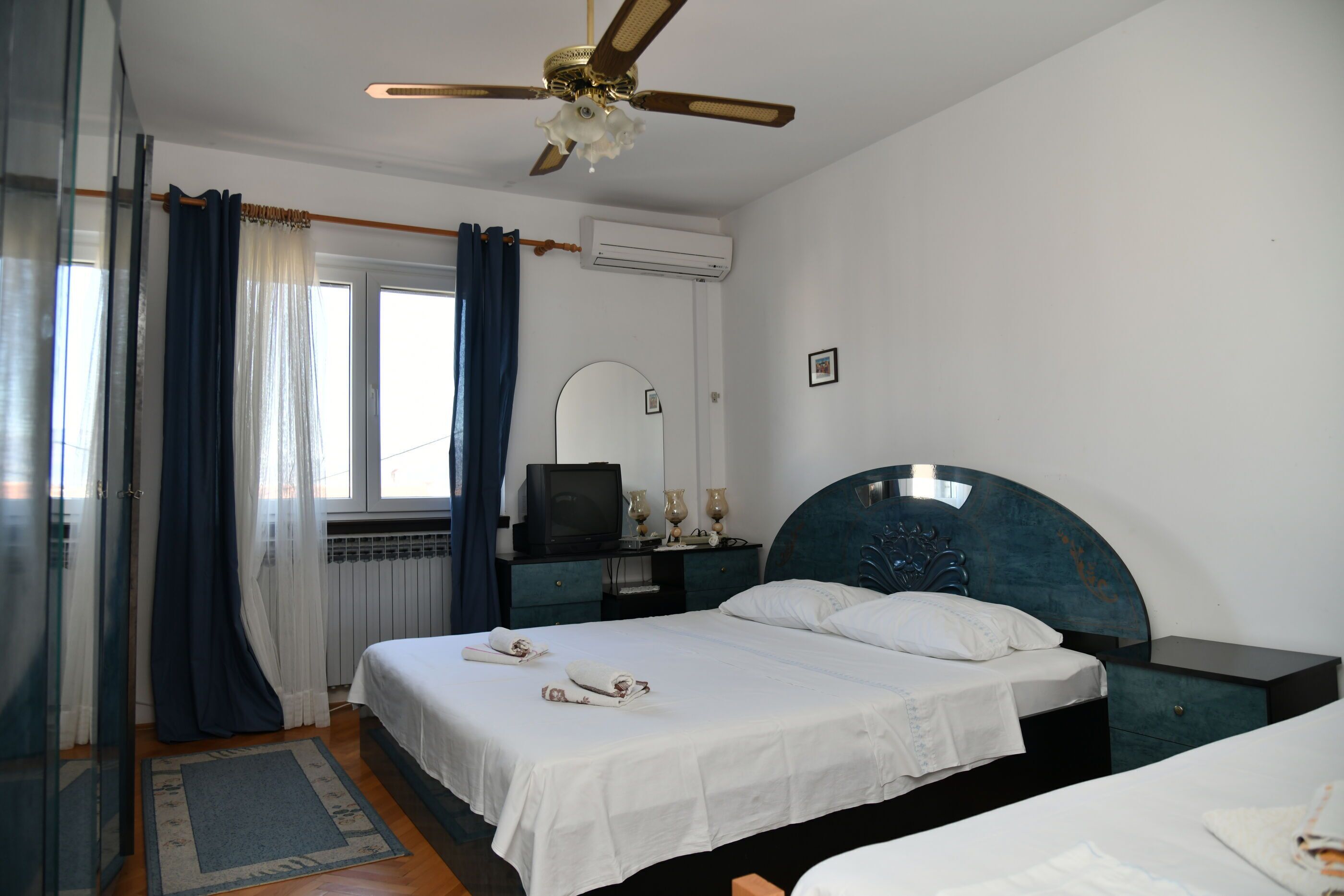 Quarto de hotel com cama, televisão, ventoinha no teto e janela com cortinas.