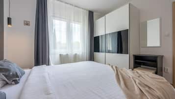 Quarto de hotel moderno com uma cama grande, uma mesinha de cabeceira, um espelho e uma janela com cortinas.