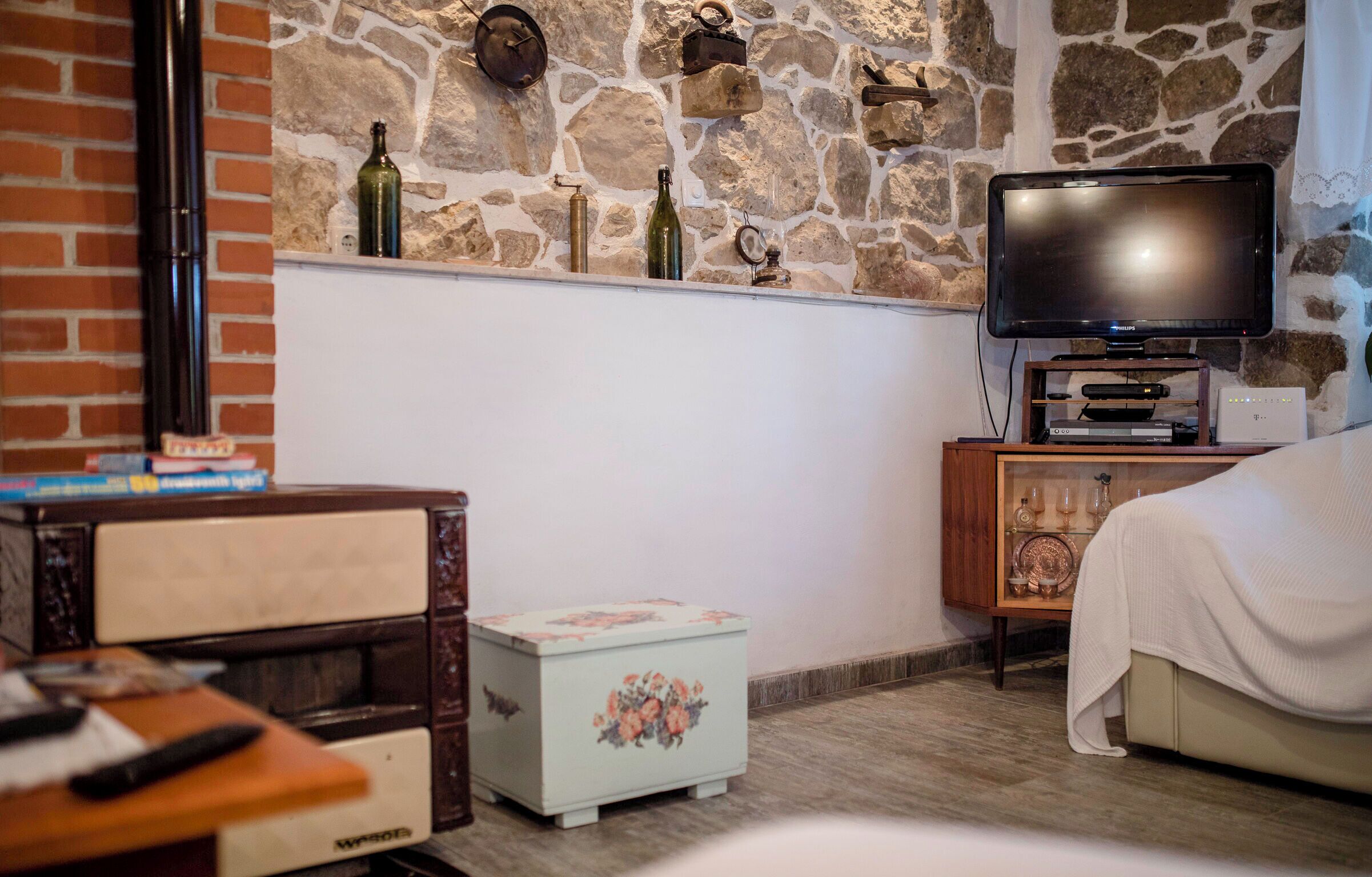 Quarto com parede de pedra, televisão, pequeno armário, cómoda com detalhes florais e uma cama.