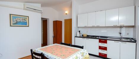 Uma cozinha compacta com armários brancos, uma mesa de jantar com toalha de mesa florida e uma cadeira de madeira.
