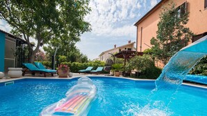 Uma piscina com uma espreguiçadeira flutuante, cadeiras de praia e um tobogã.