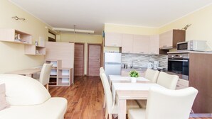 Cozinha moderna com armários de madeira, micro-ondas e forno embutido. Há uma área de refeições com mesa e cadeiras, e um sofá na sala de estar.