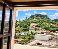 Vista da janela com um morro, edifícios e vegetação.