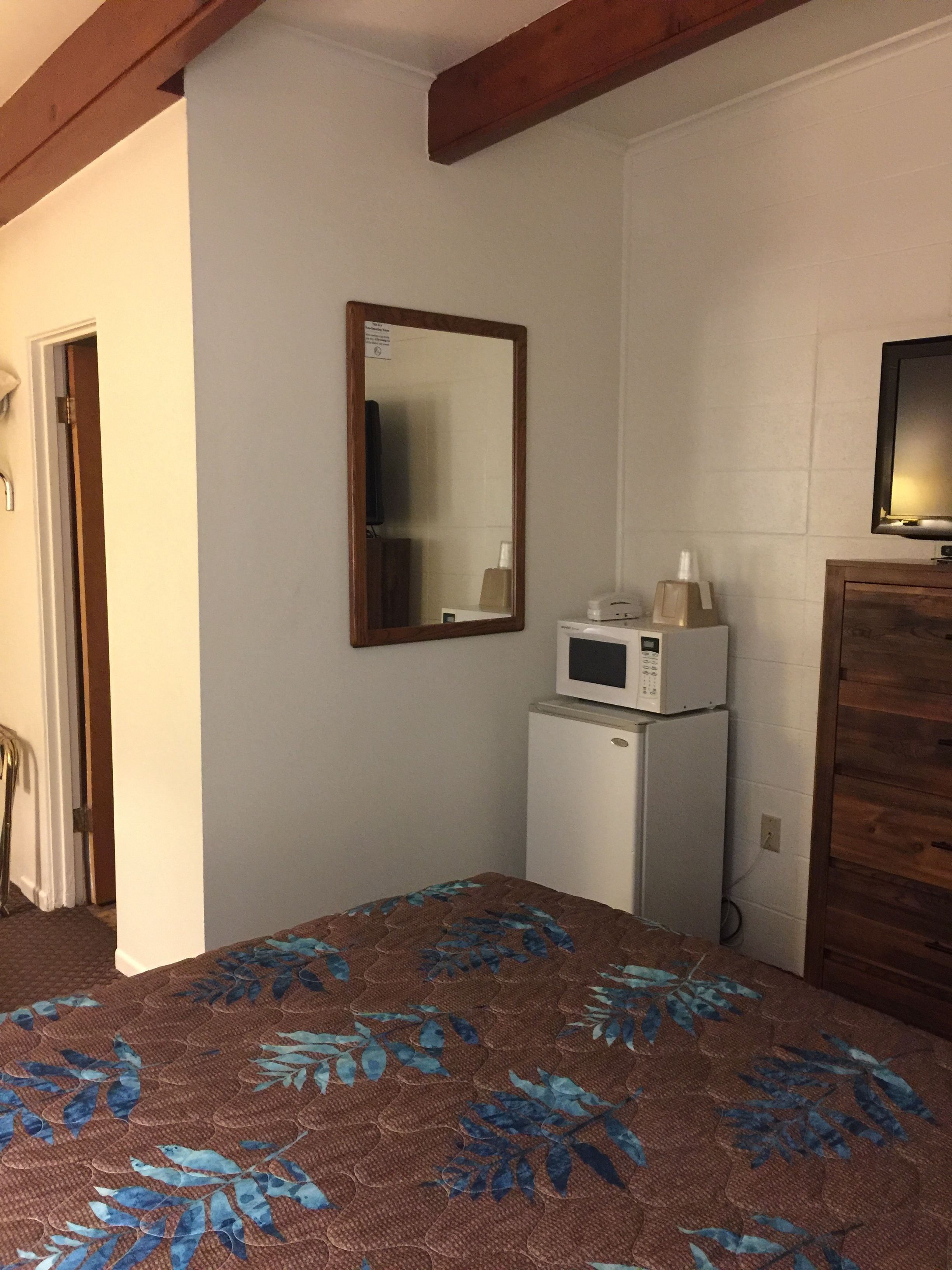 Quarto com cama, espelho, micro-ondas e armário de madeira.