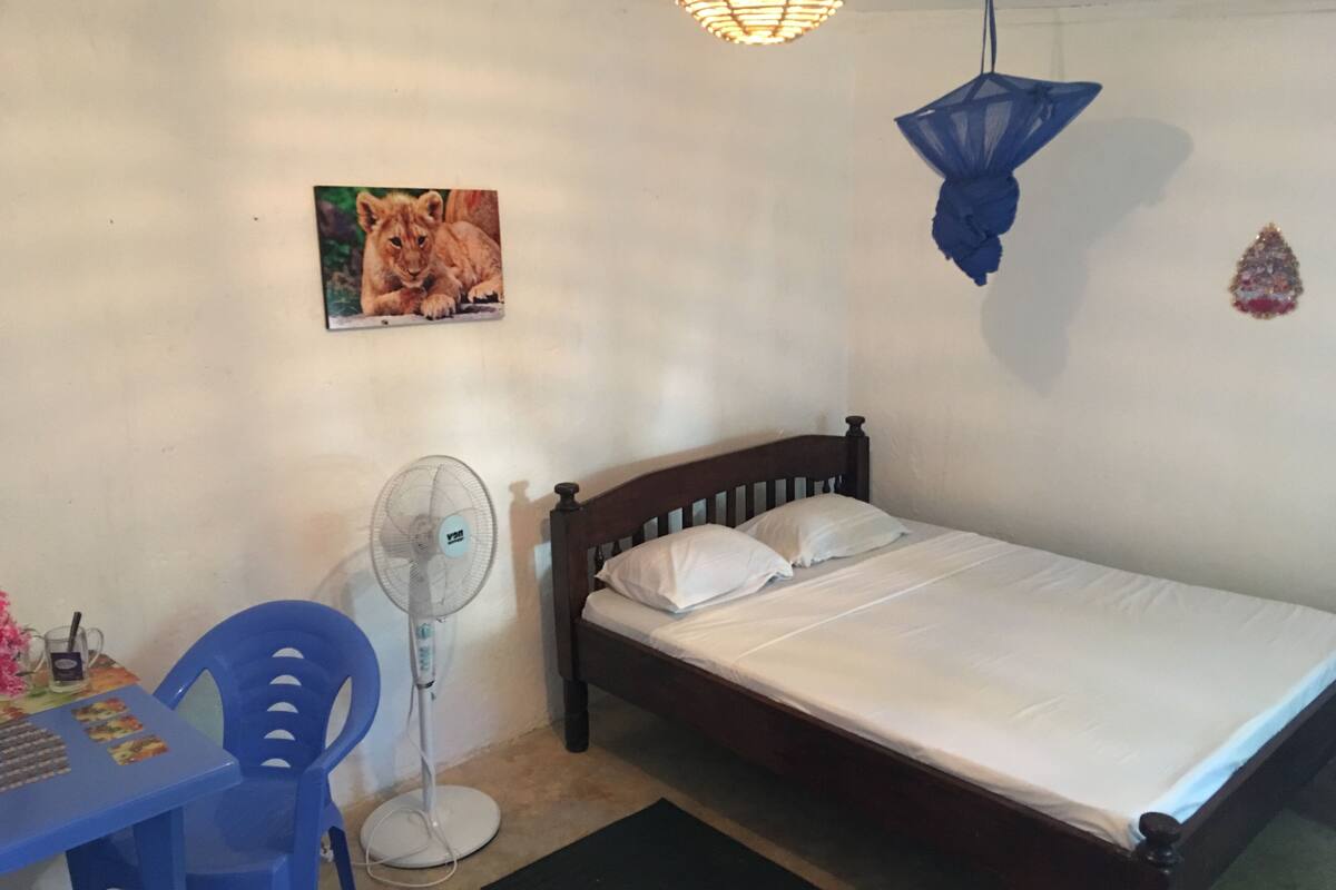 Quarto com cama, escrivaninha com cadeira, ventoinha e luminária fixada na parede.