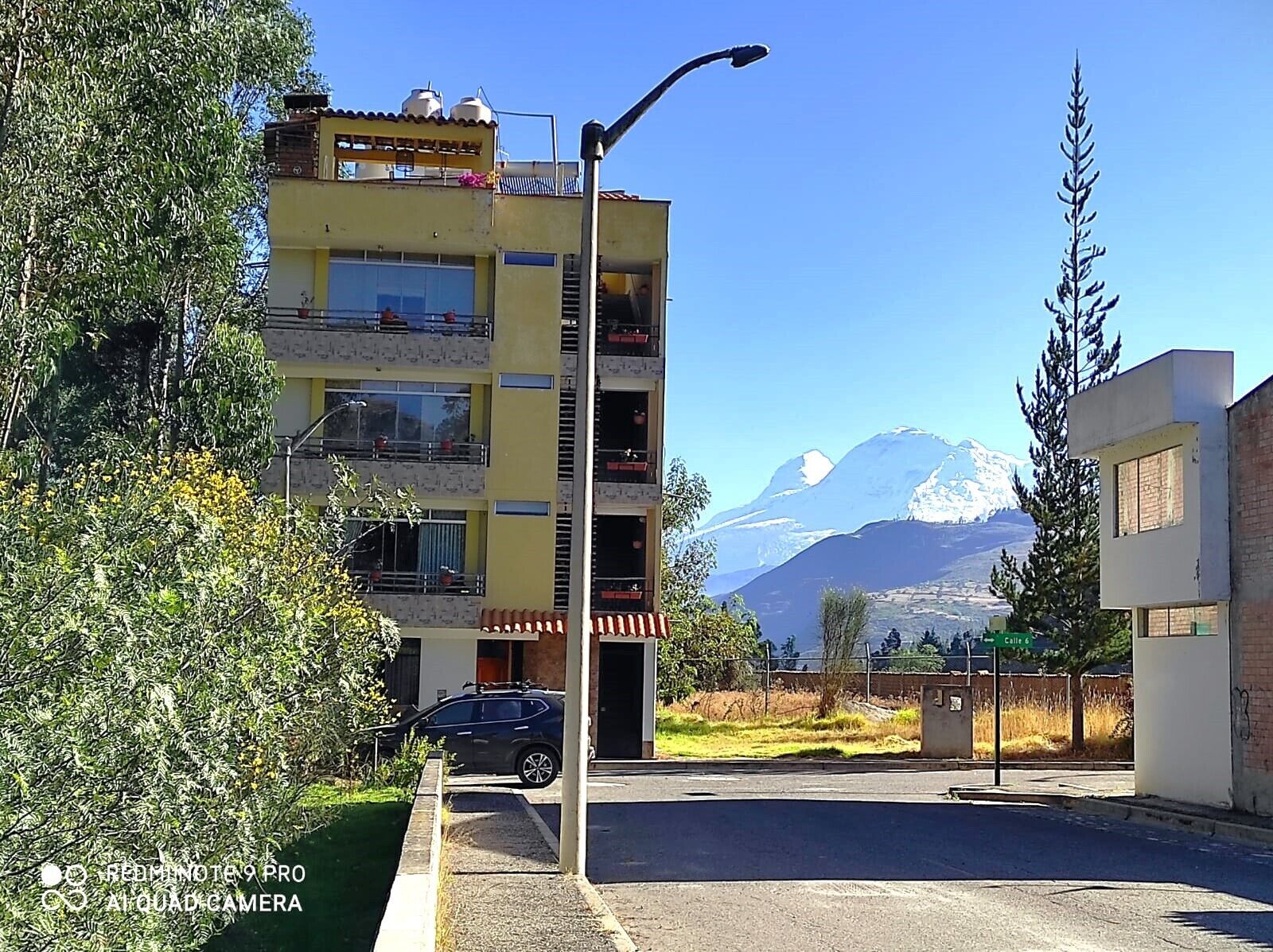Um edifício com várias andares, varandas, um carro estacionado e uma montanha ao fundo.