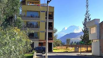 Um edifício com várias andares, varandas, um carro estacionado e uma montanha ao fundo.