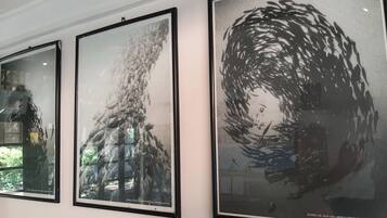 Parede com várias obras de arte emolduradas, incluindo uma grande peça em preto e branco retratando um naufrágio.