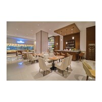 Um café moderno com mesas e cadeiras arredondadas, um espaço de bar com prateleiras cheias de garrafas e um letreiro de neon ao fundo.