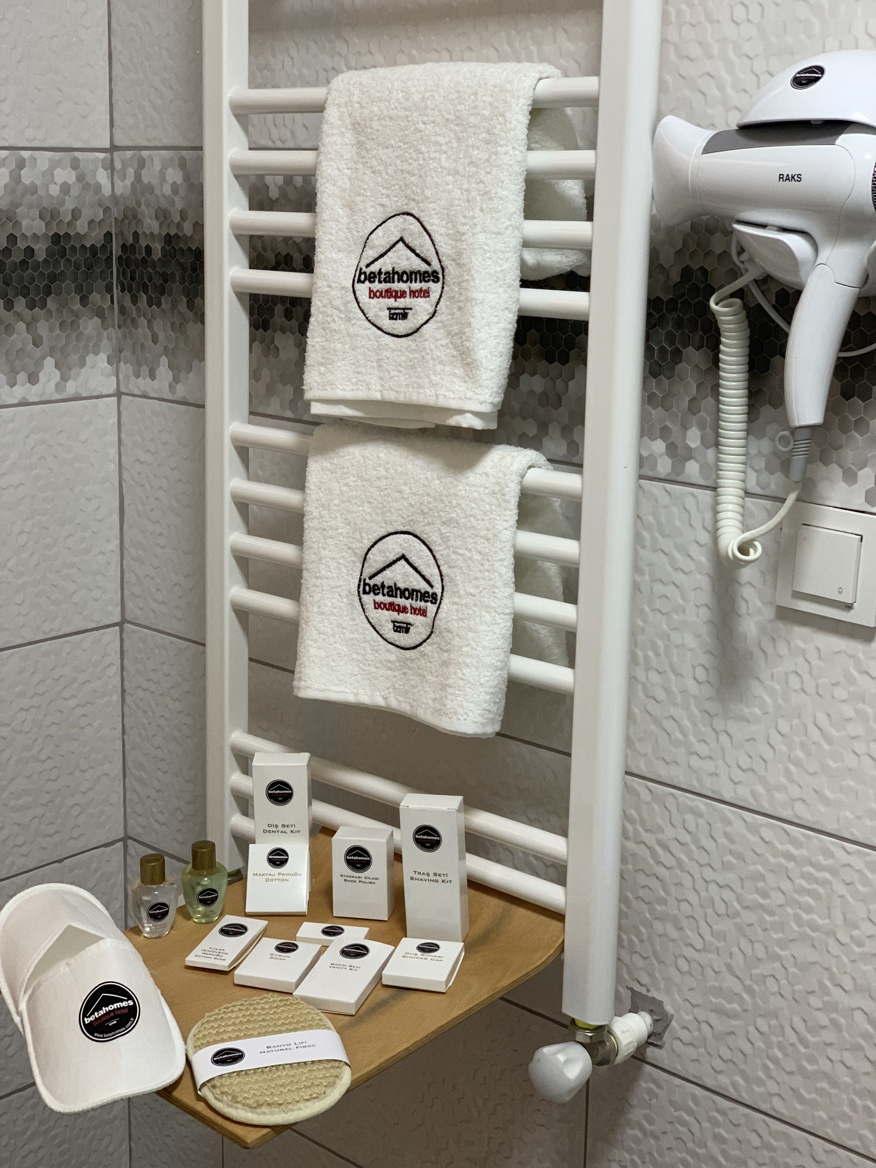 Um banheiro com porta-toalhas com duas toalhas, secador de cabelo e diversos produtos de higiene em uma prateleira.