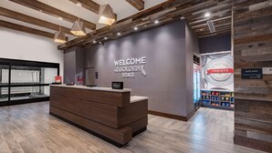 Uma área de recepção de hotel com design moderno, apresentando um balcão de madeira, uma placa de boas-vindas e uma loja de pacotes turísticos.