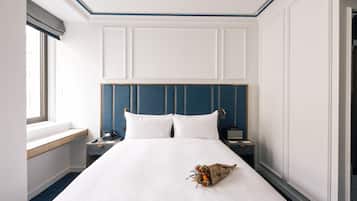 Quarto de hotel com uma cama grande, uma mesa de cabeceira com abajur, um criado-mudo e uma janela com vista.
