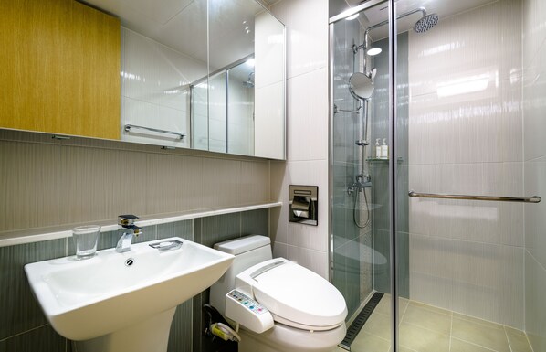 Uma casa de banho moderna com cabine de duche em vidro, lavatório branco e sanita com painel de comando.