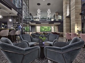 Um interior moderno com cadeiras estofadas em cinza, uma mesa central e um bar com garrafas.